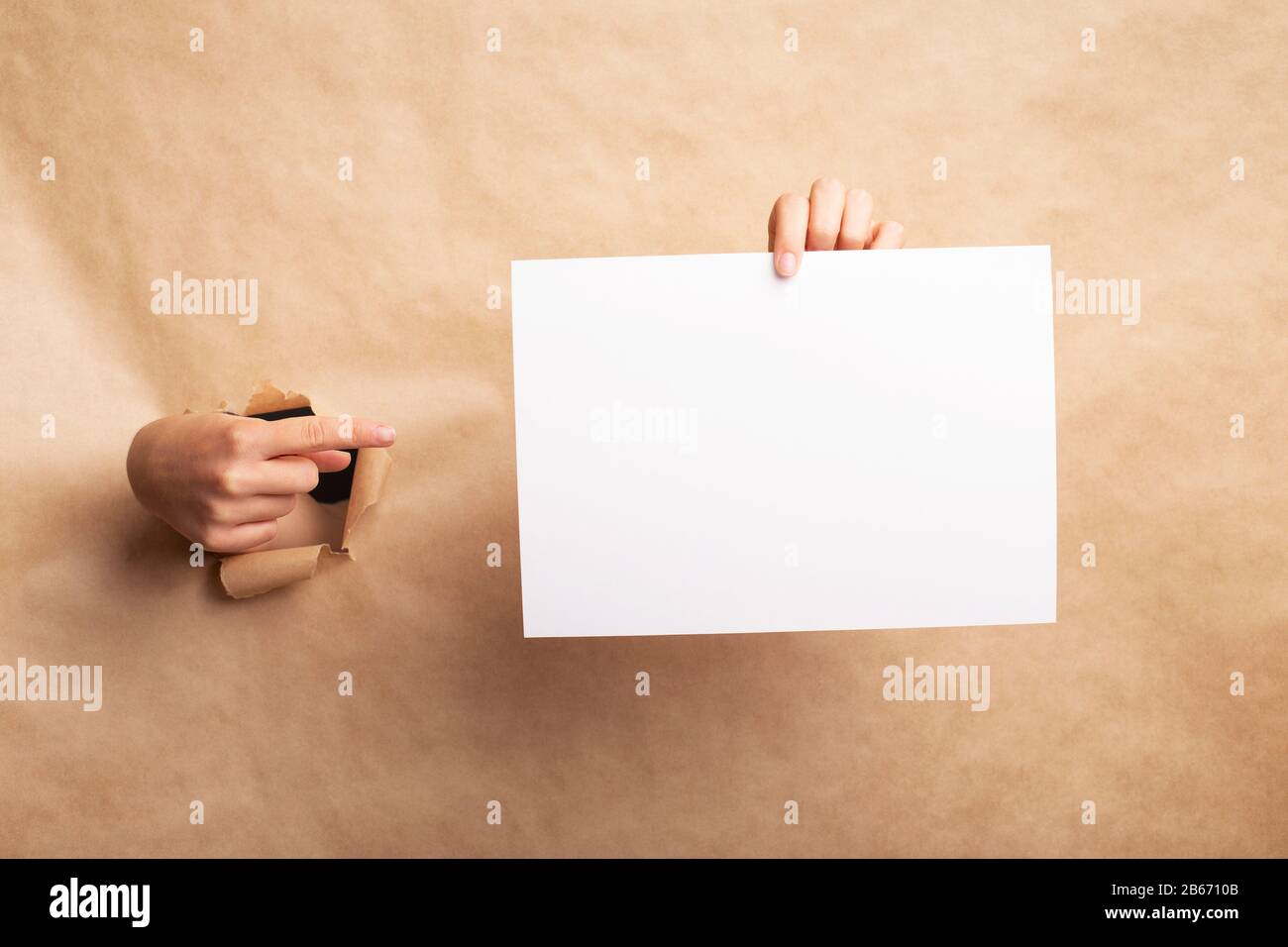 Creative idea. Woman pointing finger at empty sheet through torn brown ...