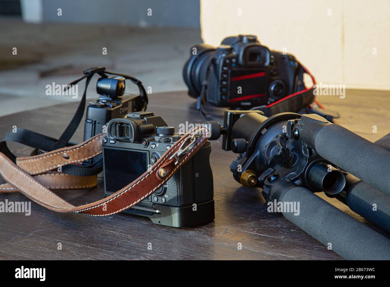 three dslr cameras and a tripod lying on a table Stock Photo - Alamy