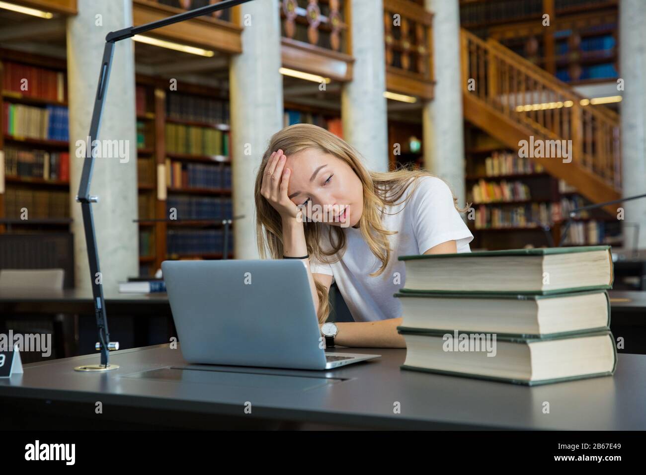 Young girl sitting at a desk in library, working at computer. Reading ...