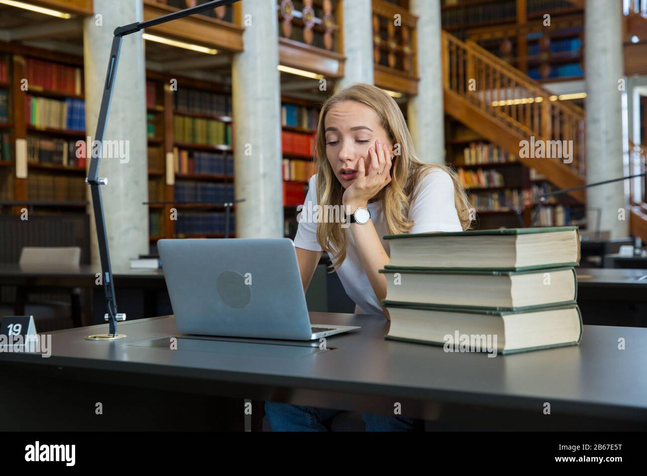 Young girl sitting at a desk in library, working at computer. Reading ...
