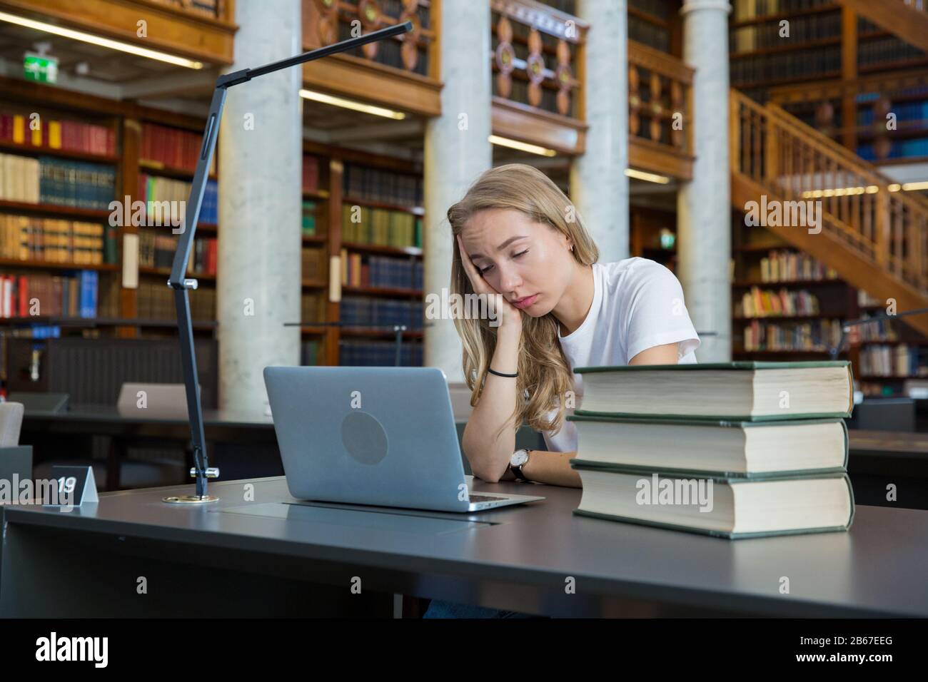 Young girl sitting at a desk in library, working at computer. Reading ...