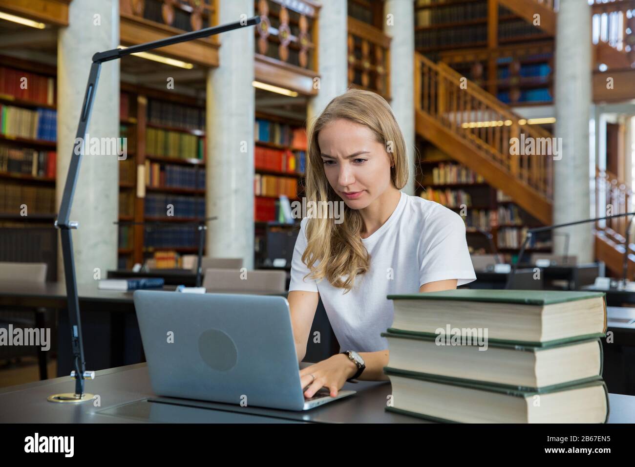 Young girl sitting at a desk in library, working at computer. Reading ...