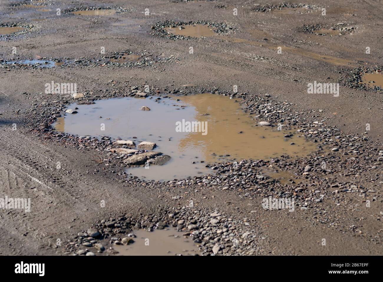A bumpy wet gravel road after the rain, gravel road is full of potholes ...
