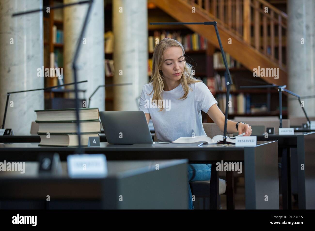 Young girl sitting at a desk in library, working at computer. Reading ...
