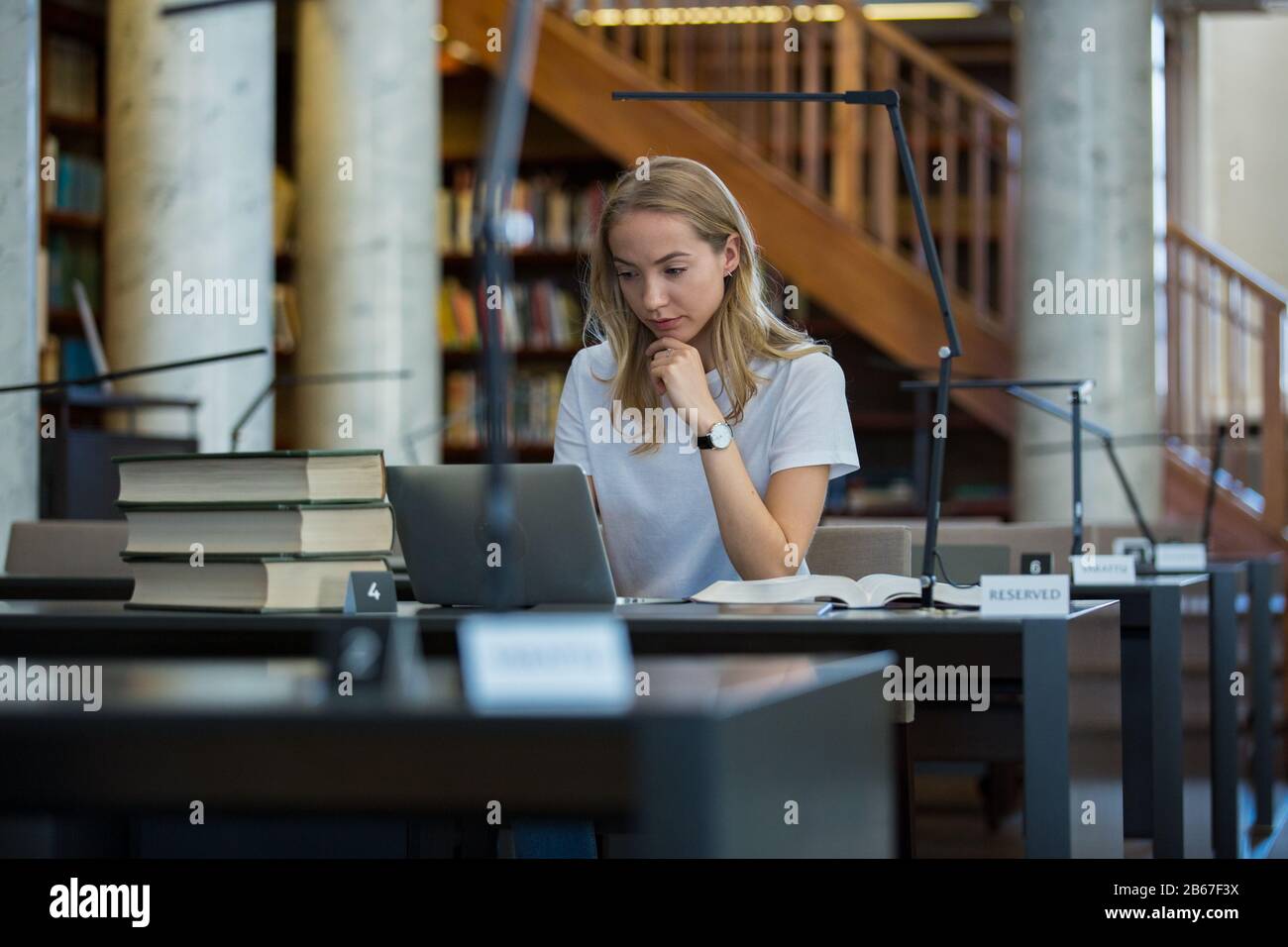 Young girl sitting at a desk in library, working at computer. Reading ...