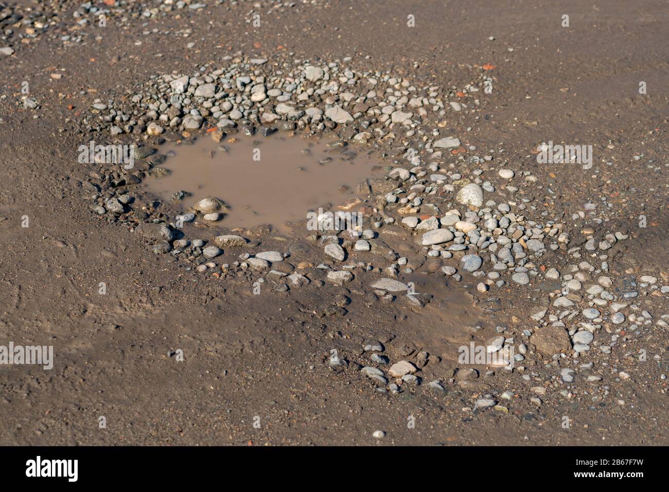 A bumpy wet gravel road after the rain, gravel road is full of potholes ...