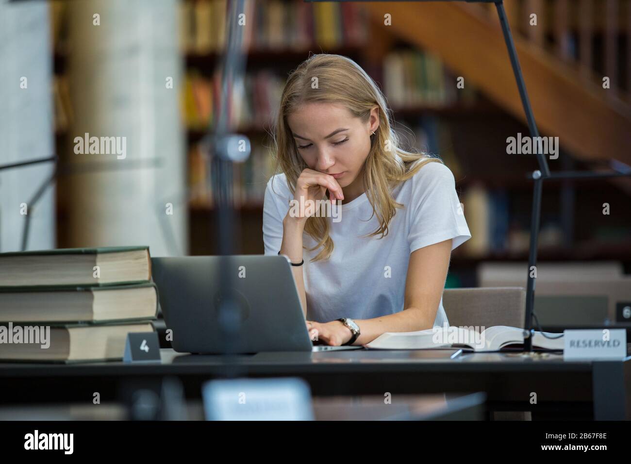 Young girl sitting at a desk in library, working at computer. Reading ...