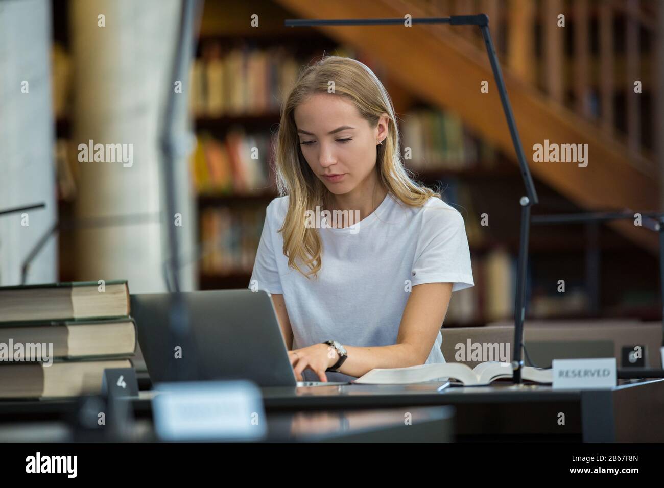 Young girl sitting at a desk in library, working at computer. Reading ...