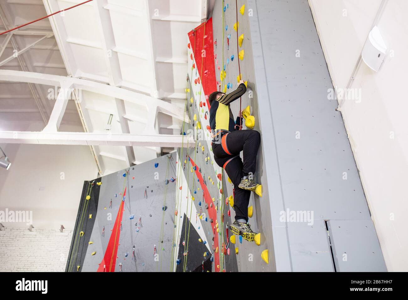 man climbing on practical wall indoor, with belay carabiners and rope ...