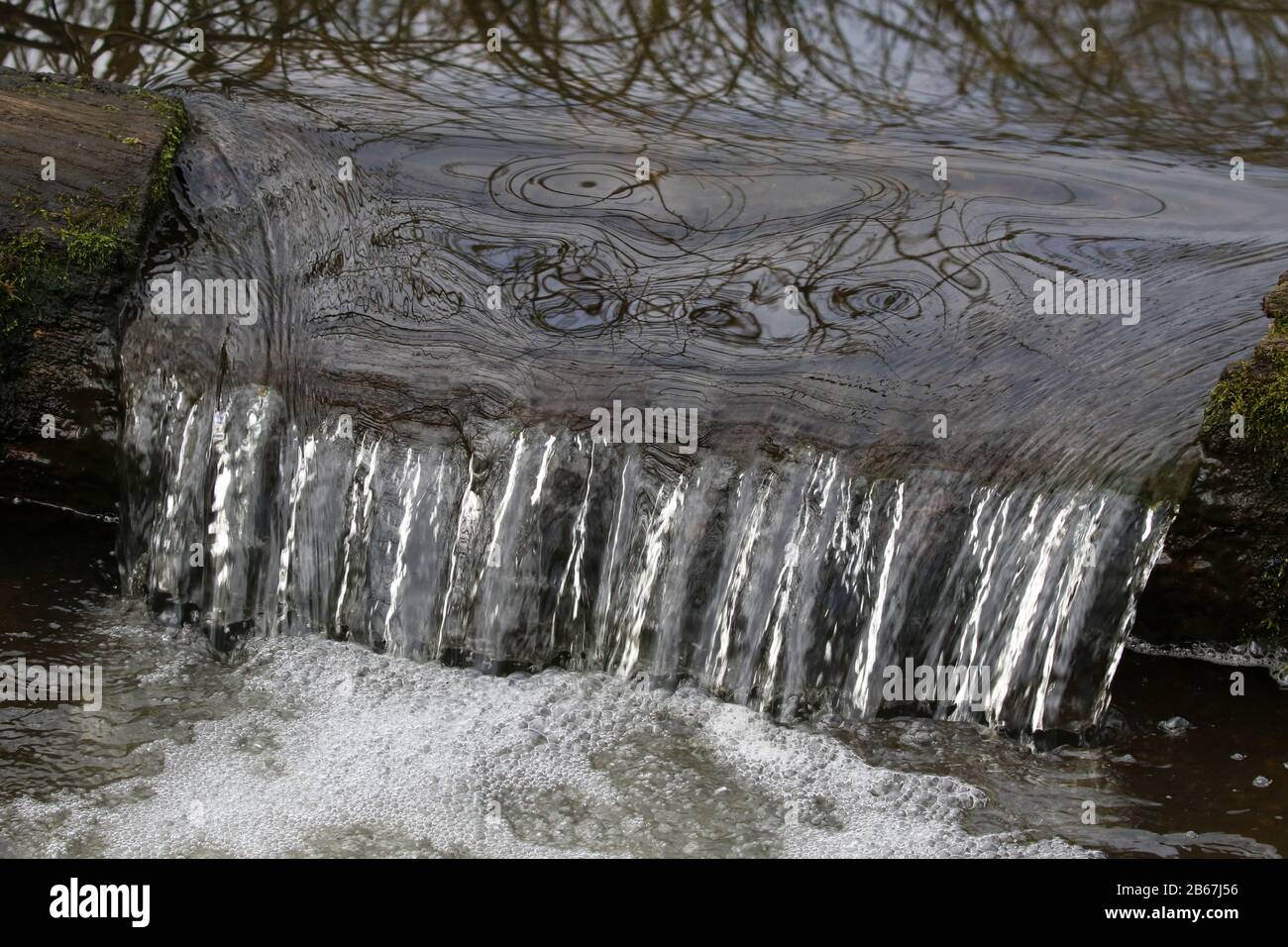 Water flowing over log with reflections Stock Photo - Alamy