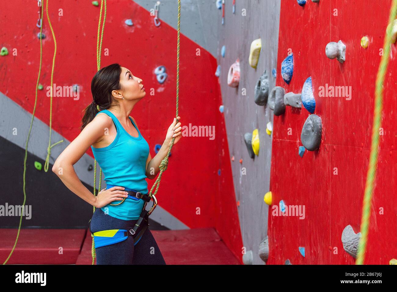 Young woman with belay rope practicing at rock-climbing on a artificial ...