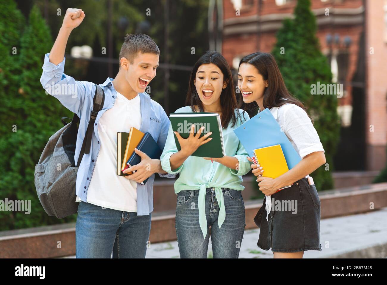 Joyful university students reading exams results standing in campus ...