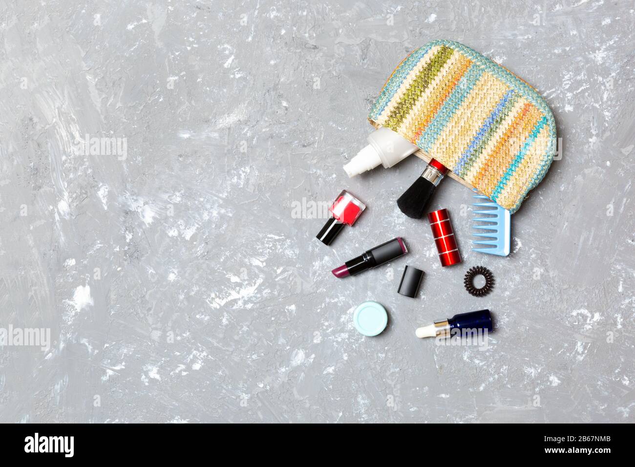 Make up products spilling out of cosmetics bag on grey cement ...