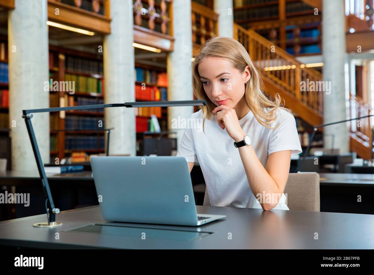 Young girl sitting at a desk in library, working at computer. Reading ...