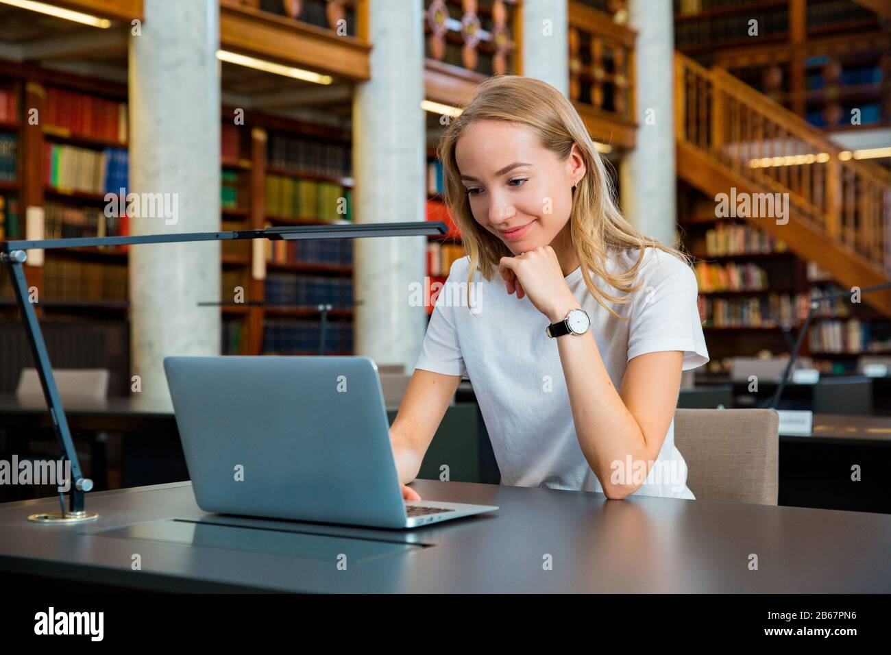 Young girl sitting at a desk in library, working at computer. Reading ...
