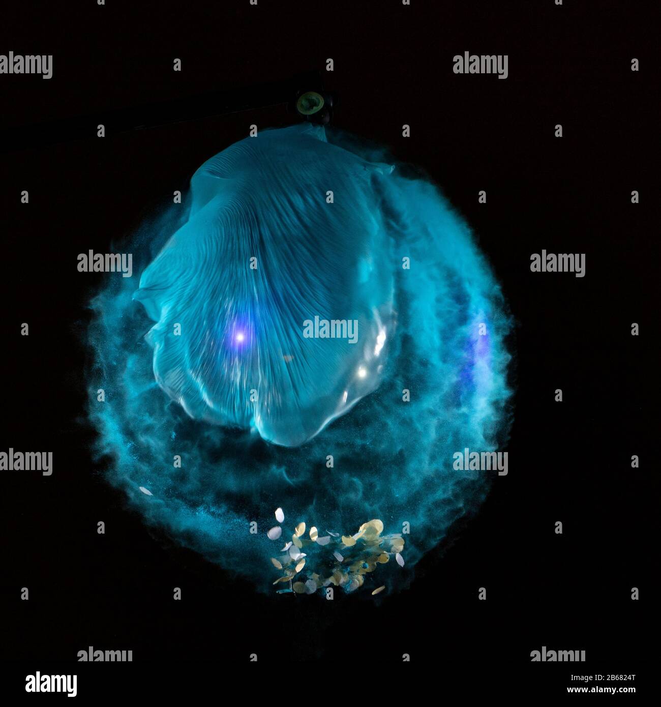 Bursting balloon full of coloured powder and glitter on a black ...