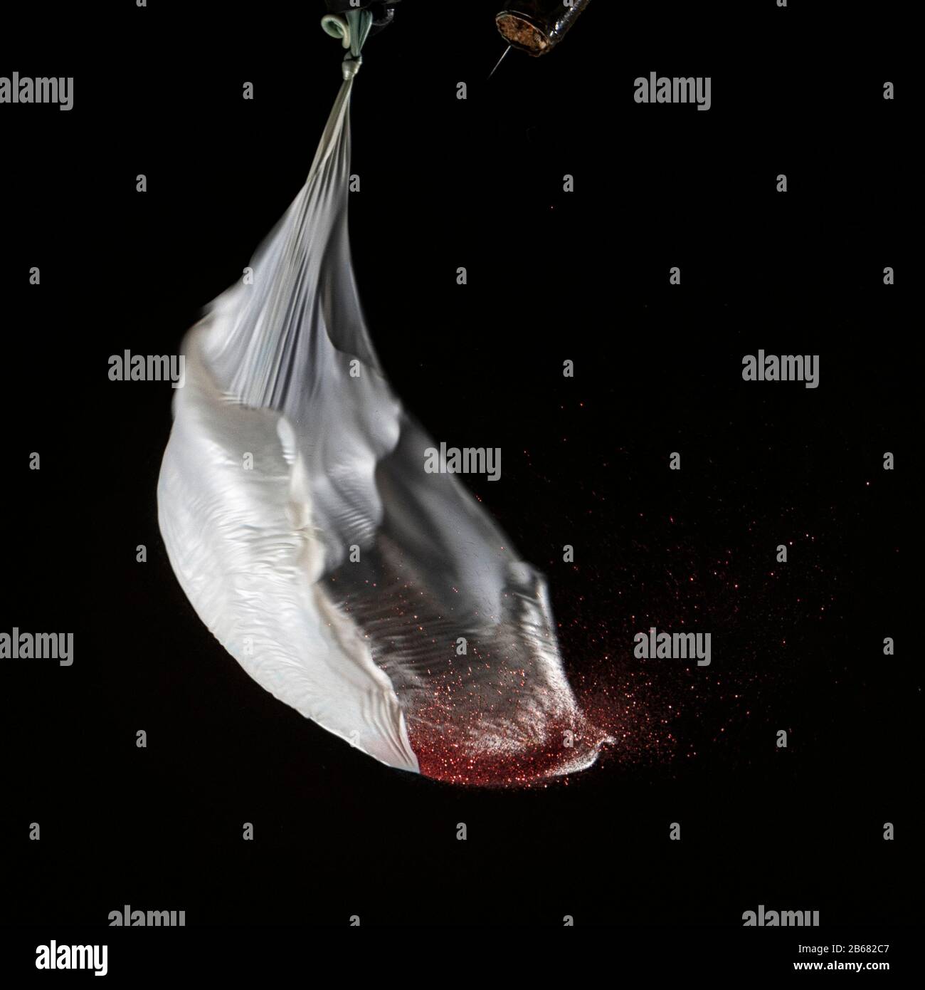 Bursting balloon full of coloured powder and glitter on a black ...