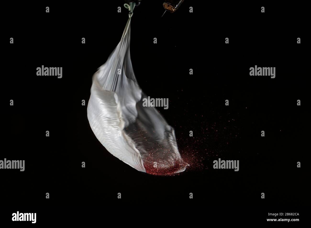 Bursting balloon full of coloured powder and glitter on a black ...