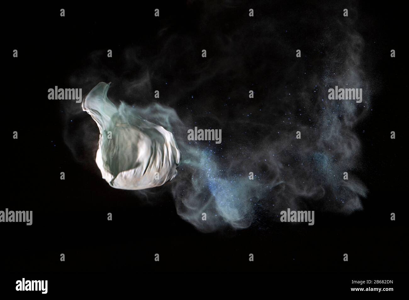 Bursting balloon full of coloured powder and glitter on a black ...