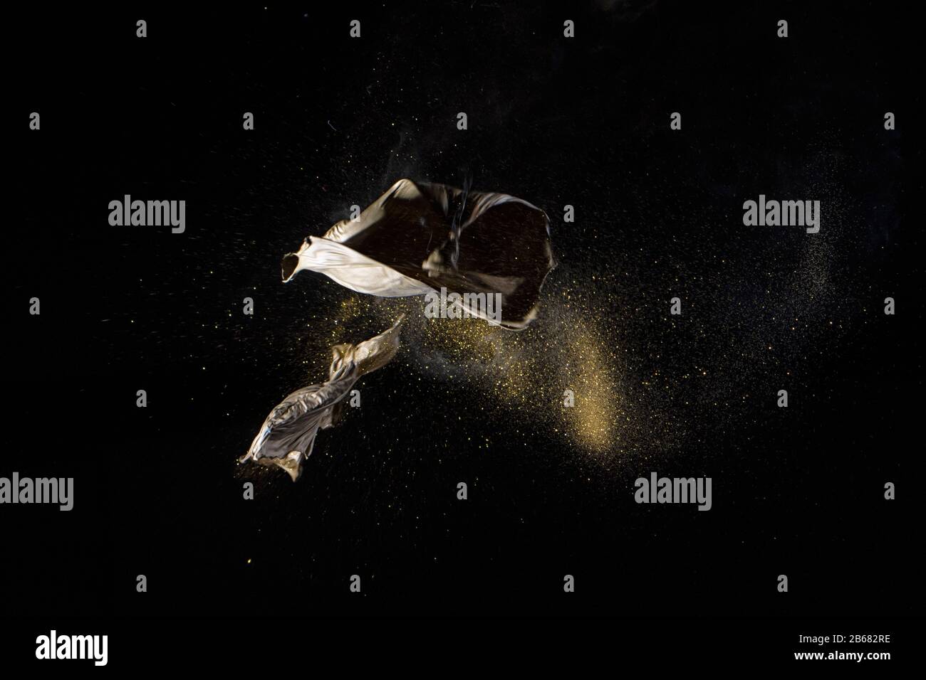 Bursting balloon full of coloured powder and glitter on a black ...