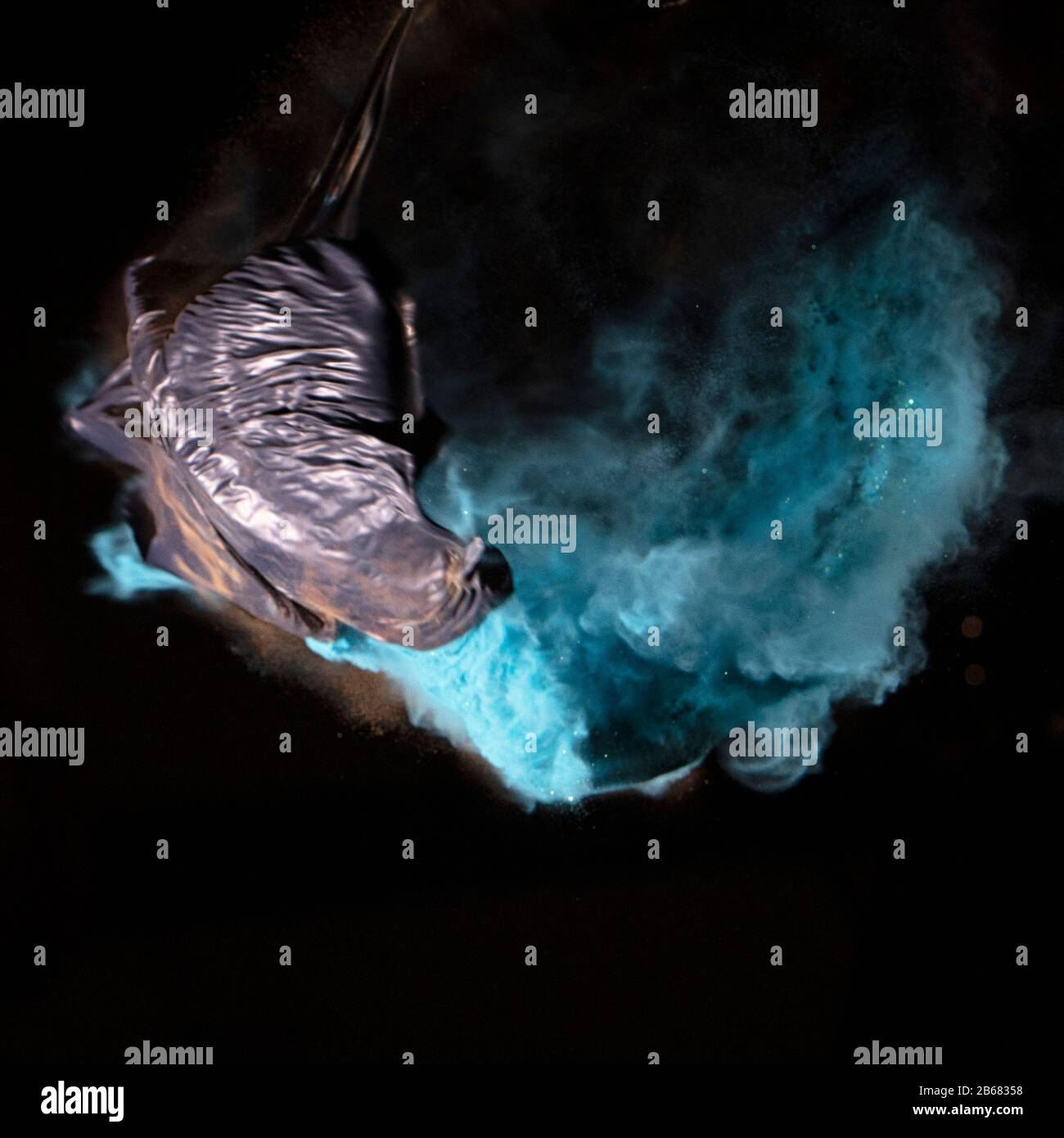 Bursting balloon full of coloured powder and glitter on a black ...