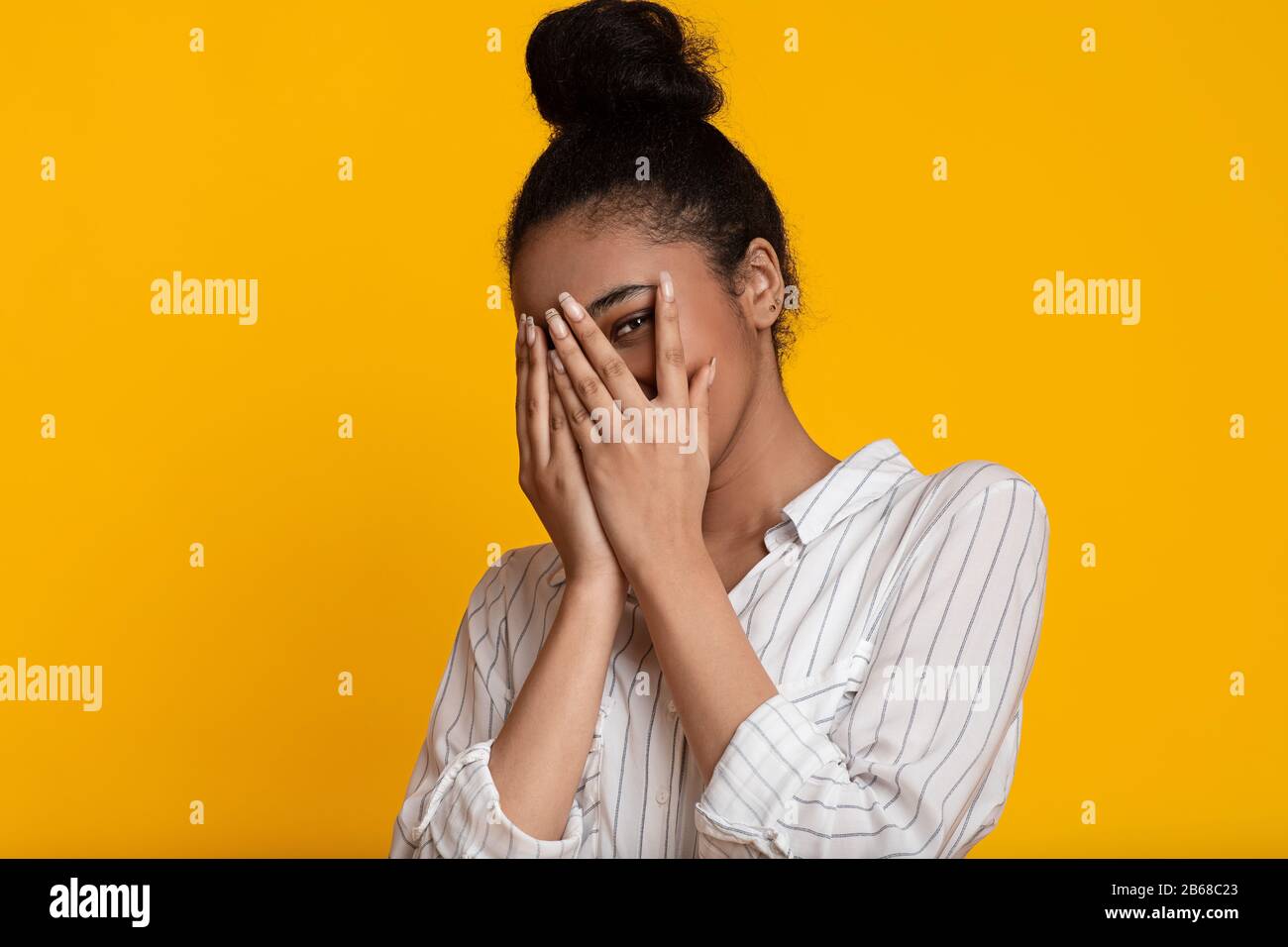 Shy afro girl covering face with hands and peeking through fingers ...