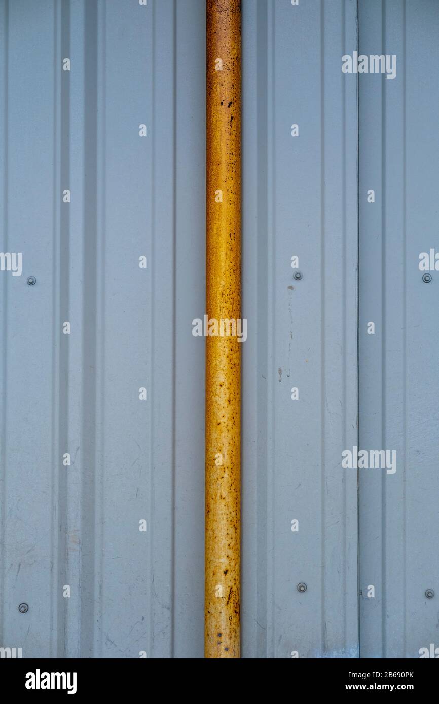 Orange gutter drain pipe against corrugated metal warehouse wall, close ...