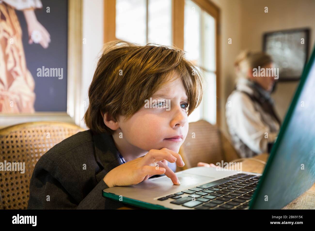 A six year old boy typing on a laptop at home, using the cursor touch ...