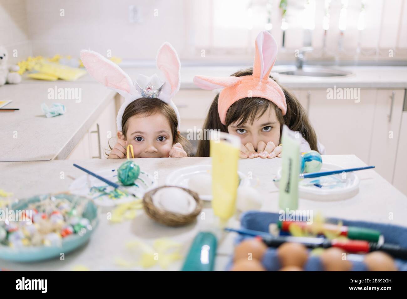 Two little girls hiding behind kitchen counter. Adorable girls in bunny ...