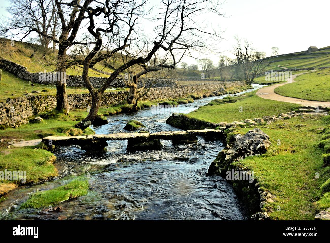 View of Malham Beck flowing downstream, with the old stone clapper ...
