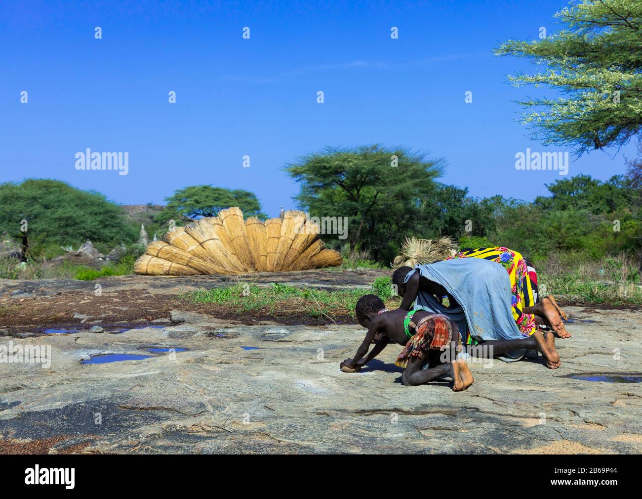 Larim tribe girls grinding sorghum grains in holes in a rock, Boya ...