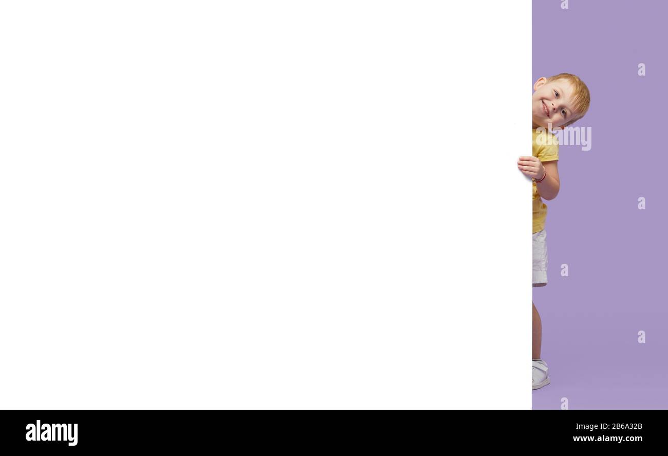 Little smiling child standing behind a white blank panel isolated ...