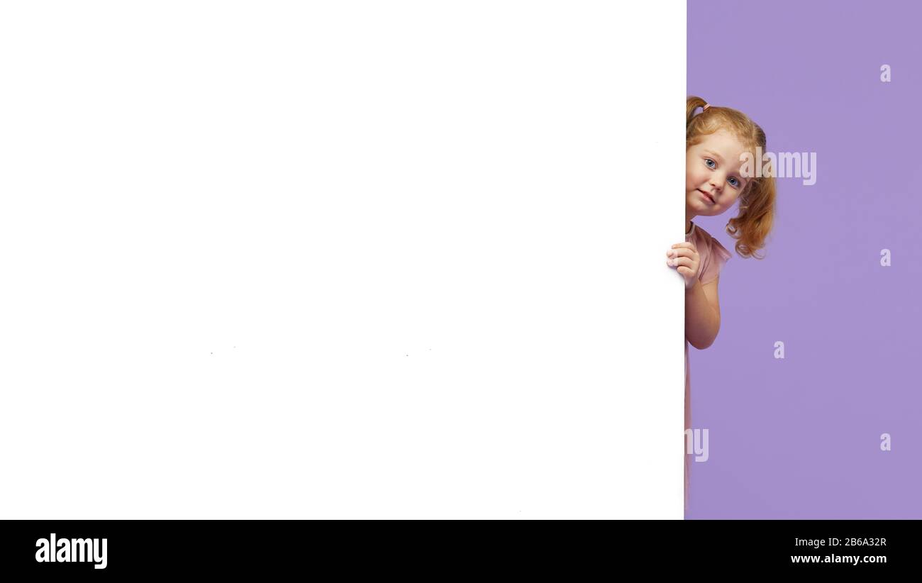 Little smiling child standing behind a white blank panel isolated ...