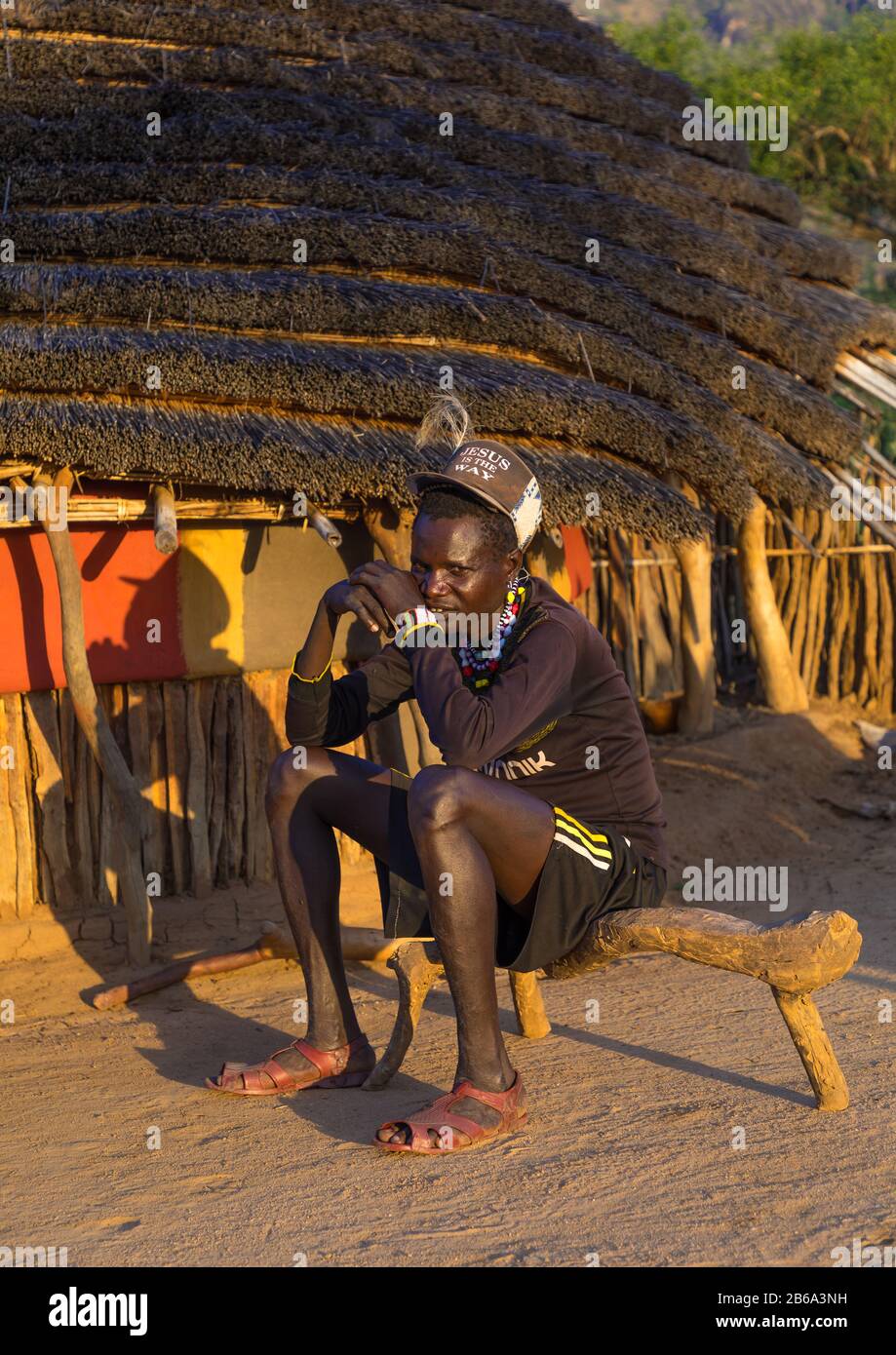 Man sit on a wooden bench in front of a Larim tribe traditional house ...