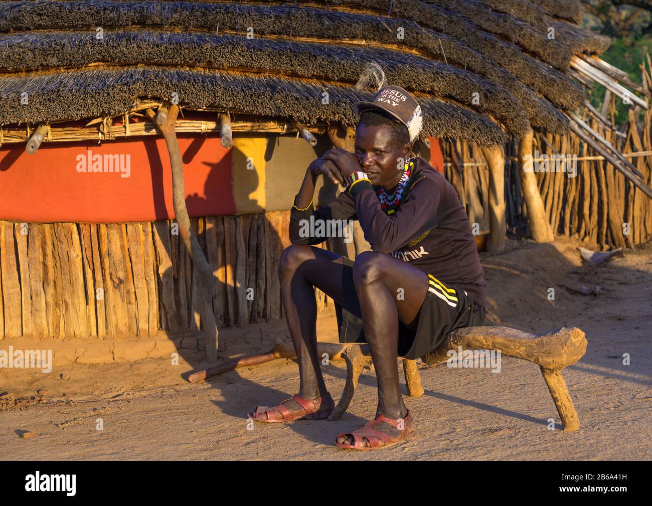 Man sit on a wooden bench in front of a Larim tribe traditional house ...