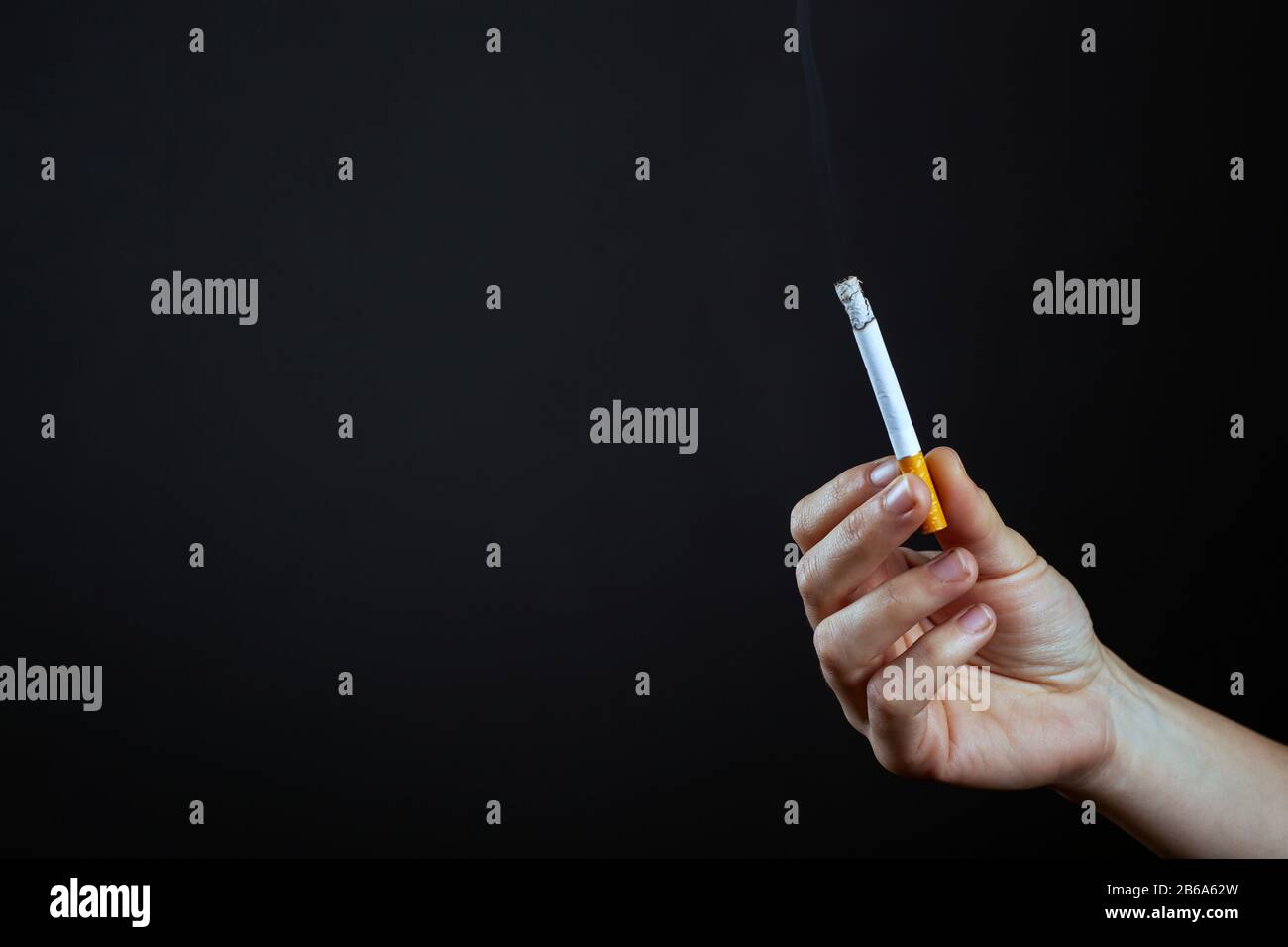 hand holds a lighted cigarette on a dark background. harm from nicotine ...
