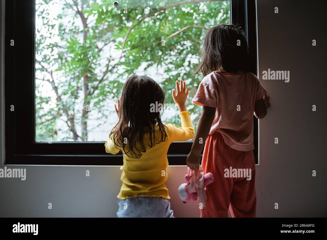 two little child seeing out of the window when standing in the bedroom ...