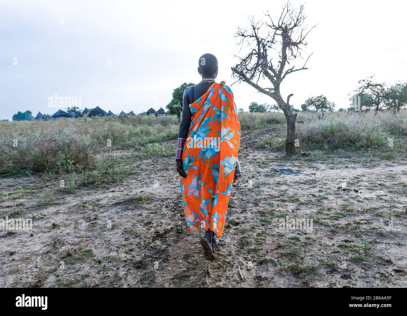 Toposa tribe woman walking on a muddy path, Namorunyang State, Kapoeta ...