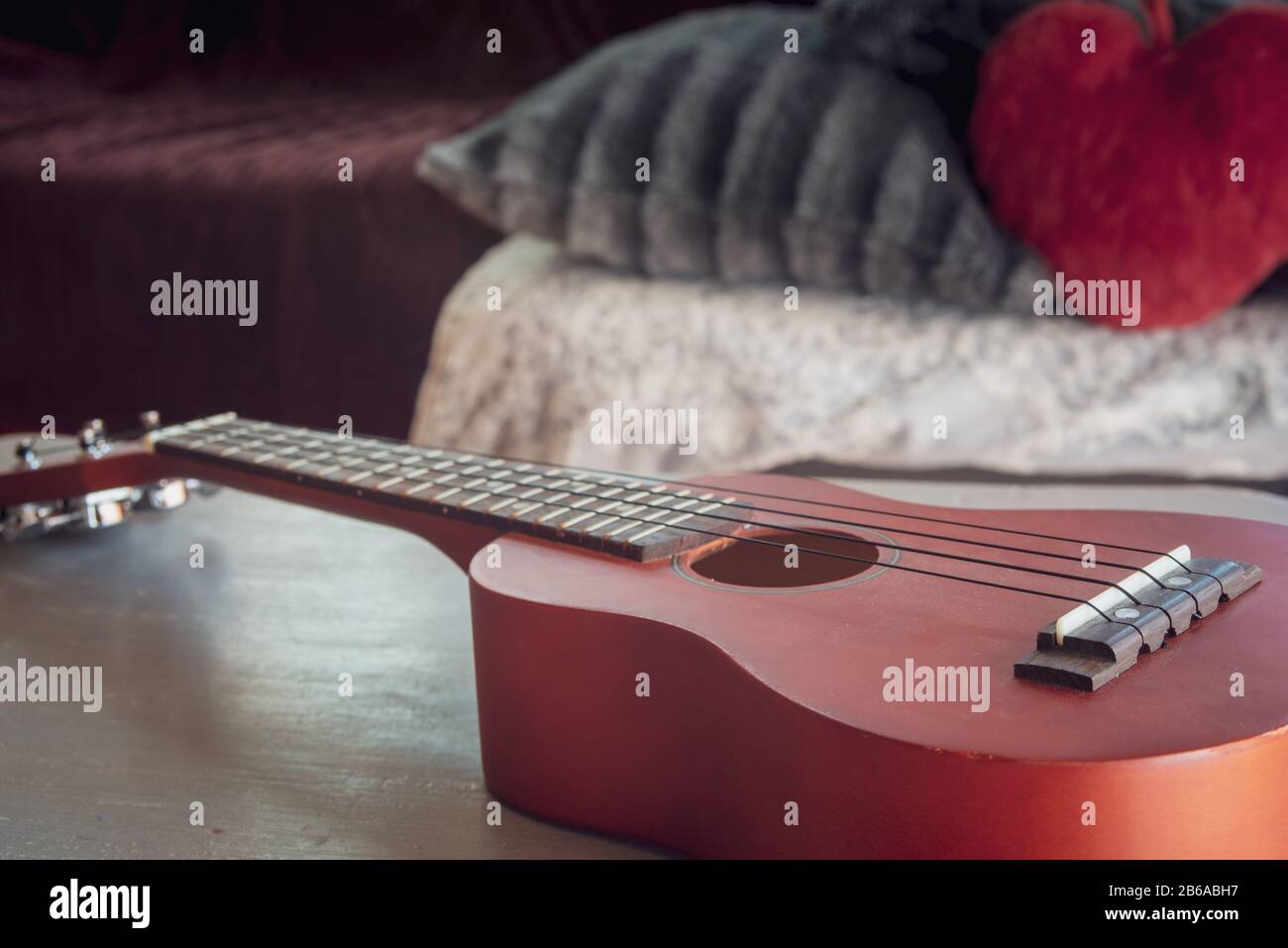 red ukulele on table with cosy room in background Stock Photo - Alamy