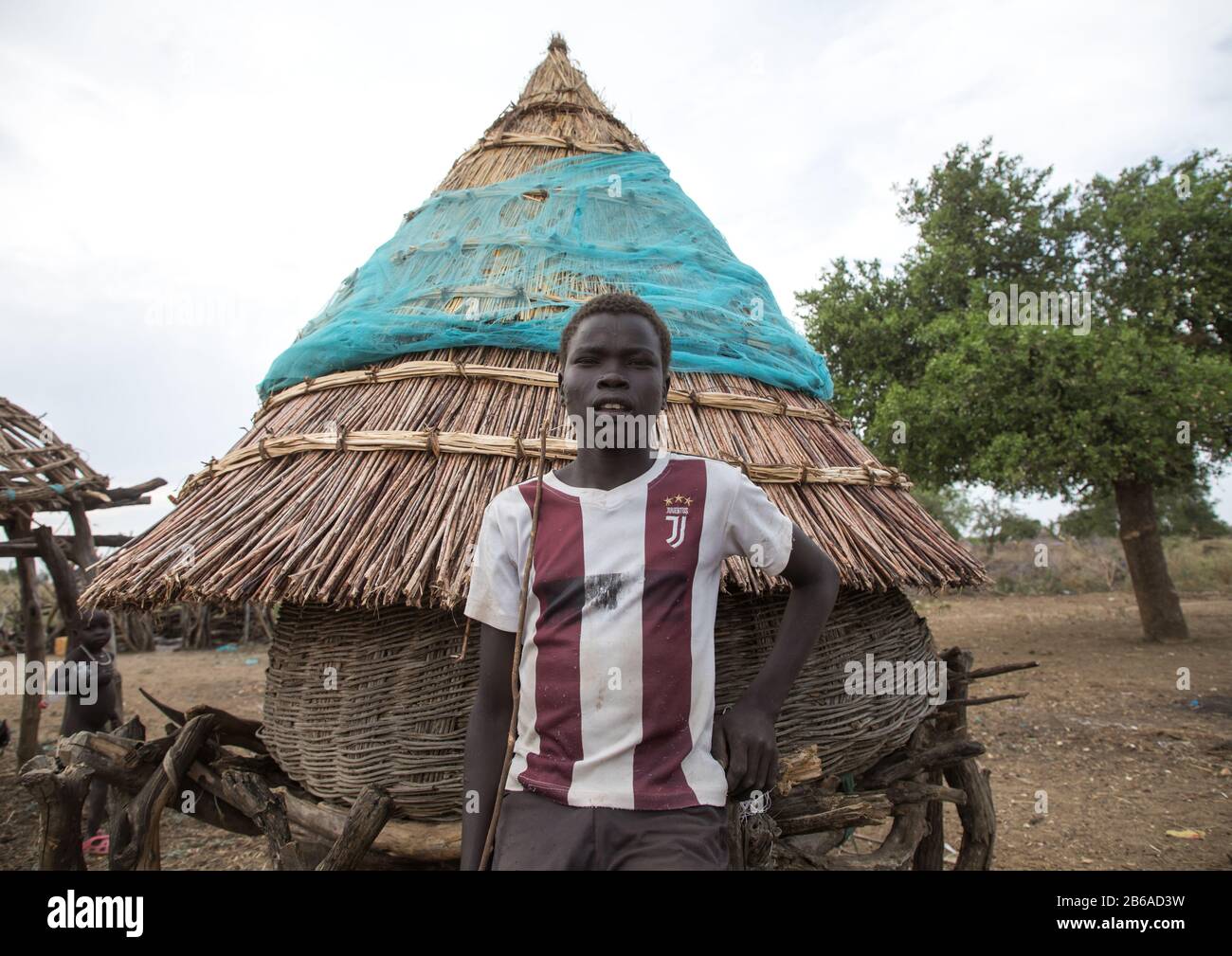 Toposa tribe boy with a Juventus football shirt standing near a granary ...