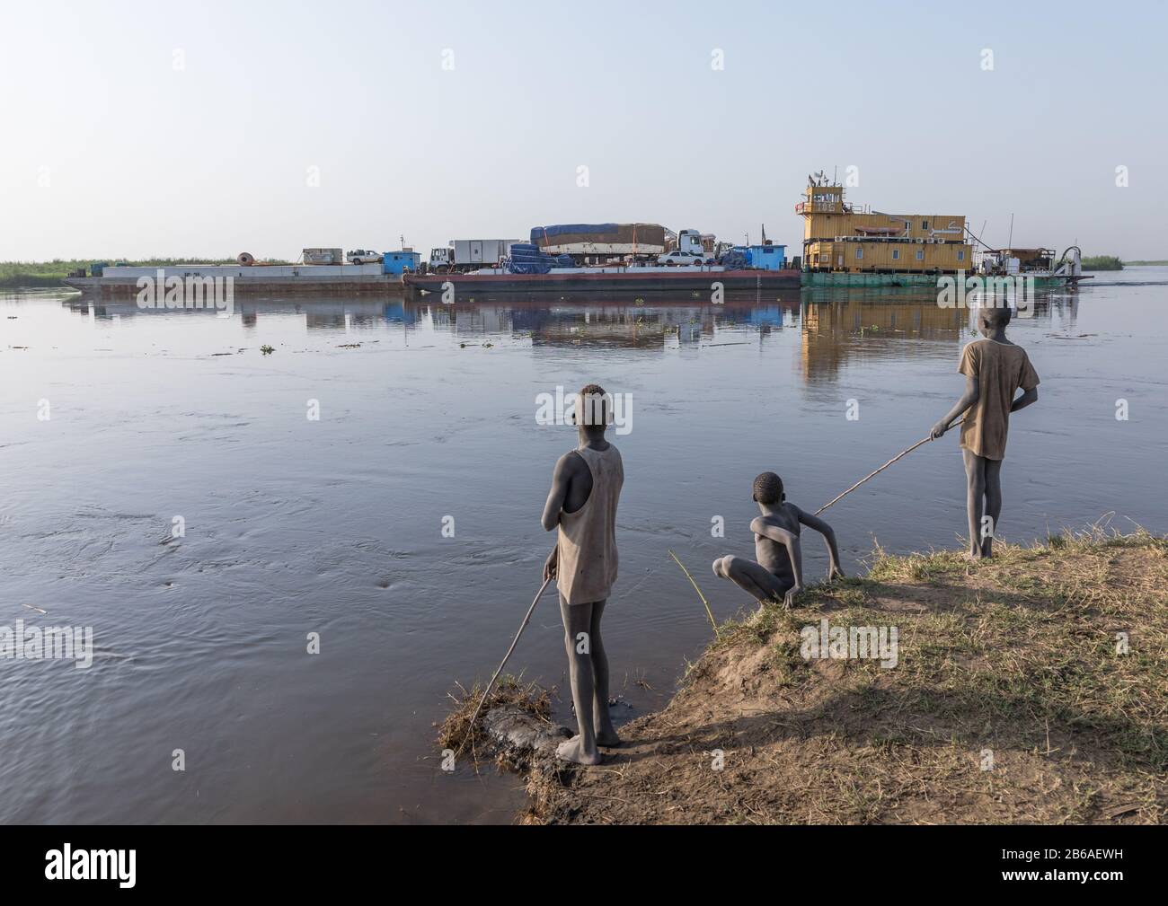 Barge passing in front of Mundari tribe boy fishing in river Nile ...