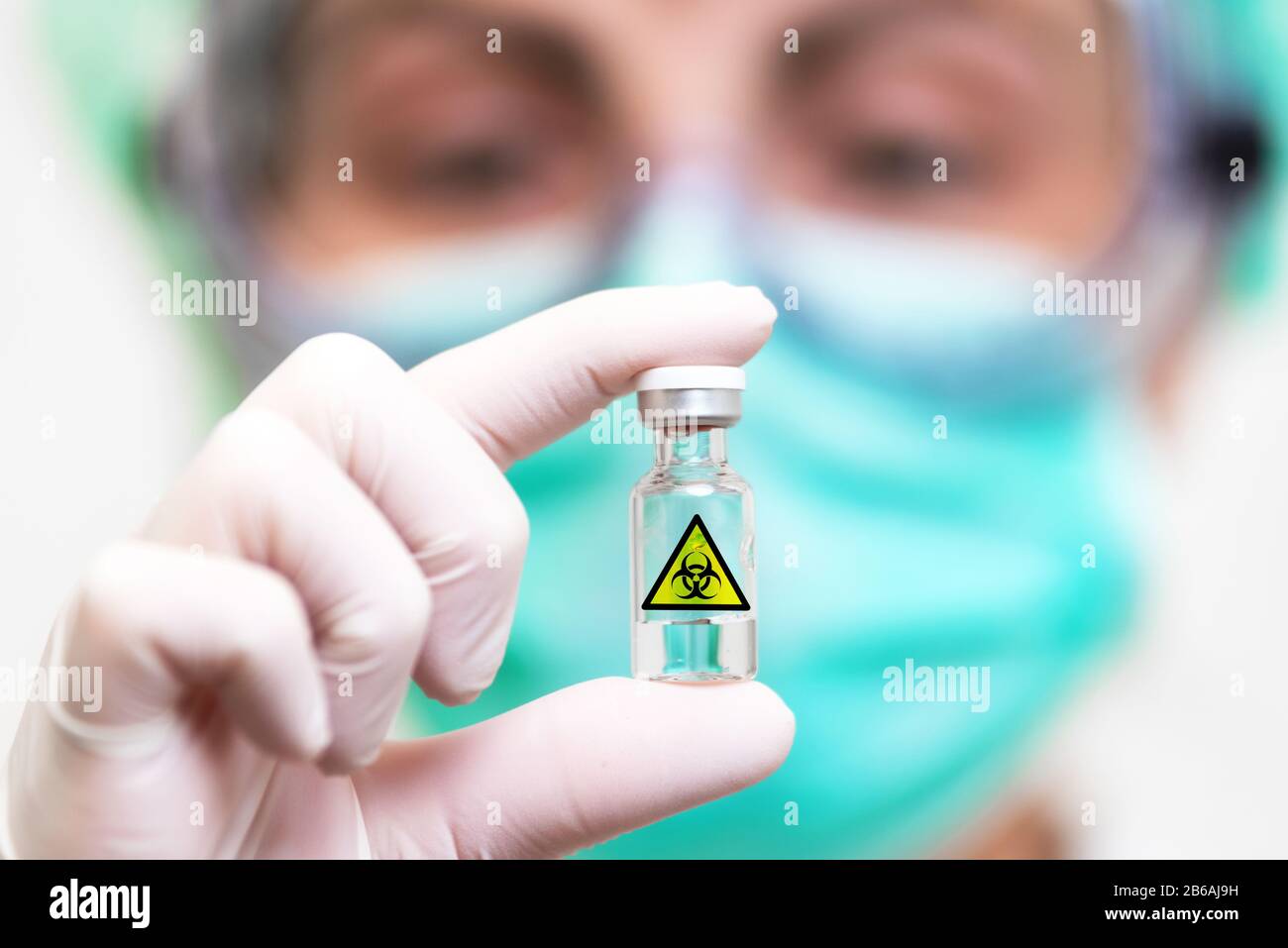 Scientist in protective mask holding sample tube with biohazard sign ...
