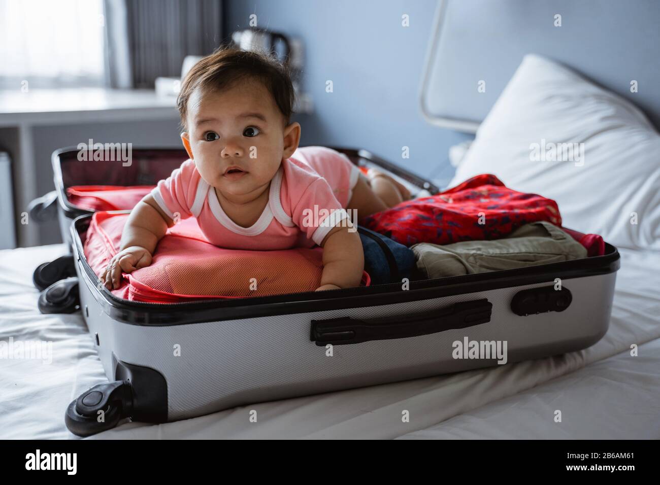 baby smiles on his stomach in an open suitcase filled with clothes ...