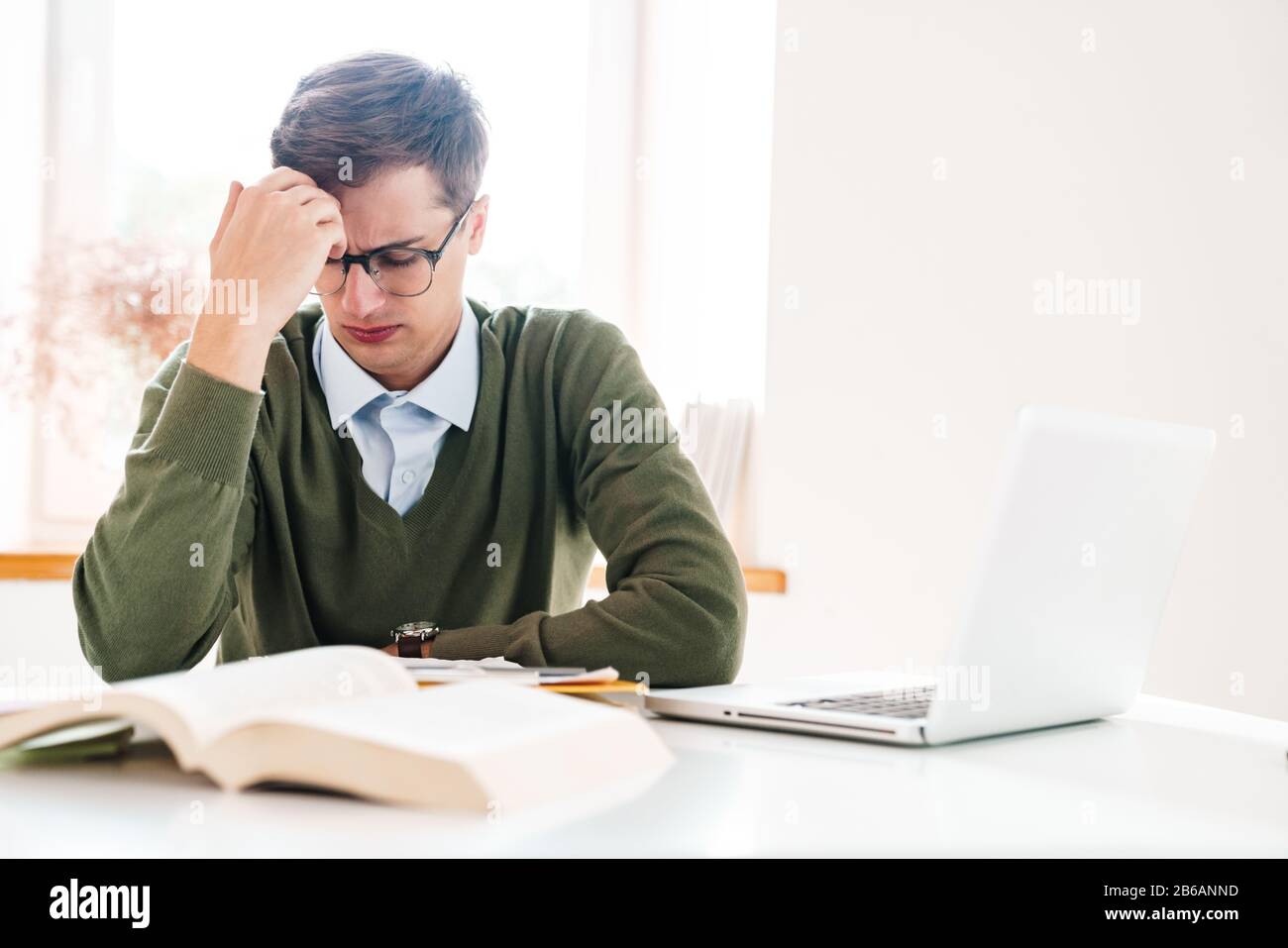 Photo of stressed tired young guy student sit at the table indoors ...