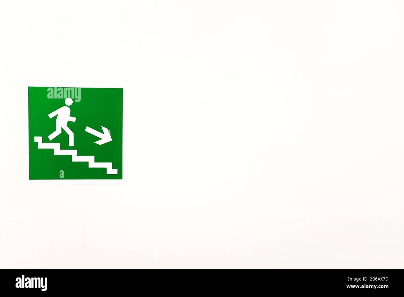 A green sign down the stairs on an empty bright wall. DIRECTION TO THE ...