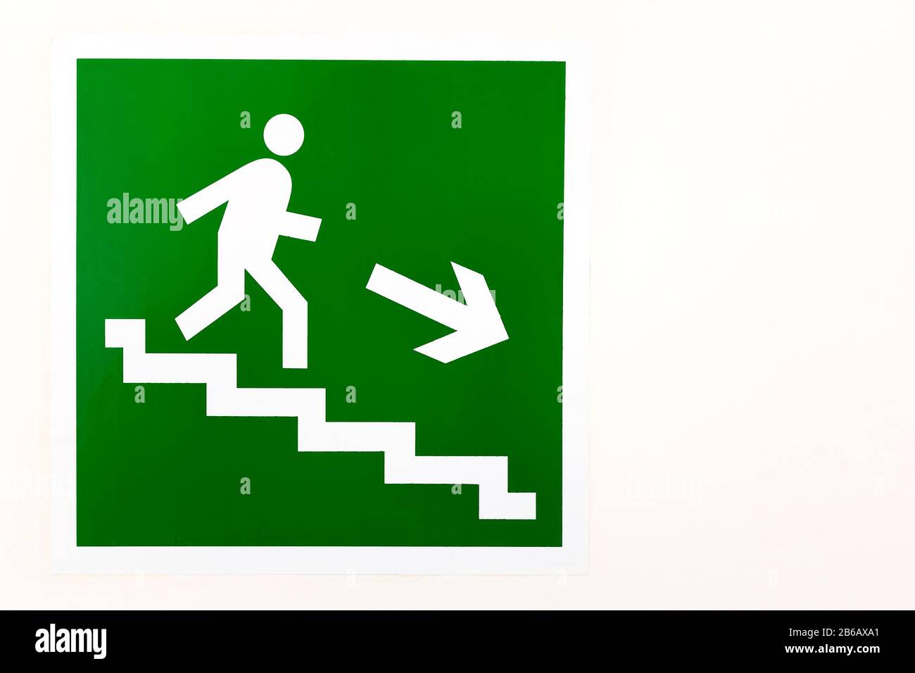 A green sign down the stairs on an empty bright wall. DIRECTION TO THE ...