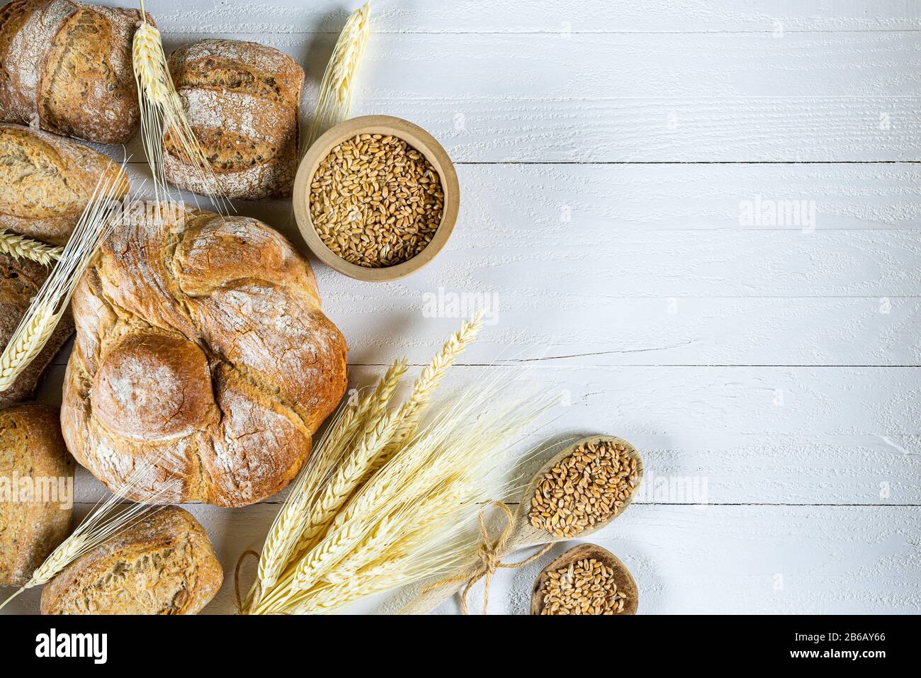 Traditional wheat bread, rolls and ears of cereals on a white wooden ...