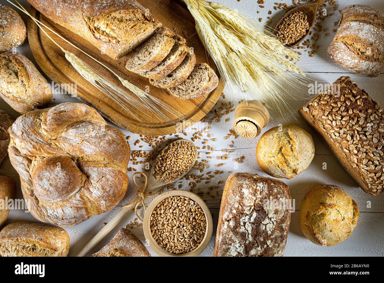 Traditional wheat bread, rolls and ears of cereals on a white wooden ...