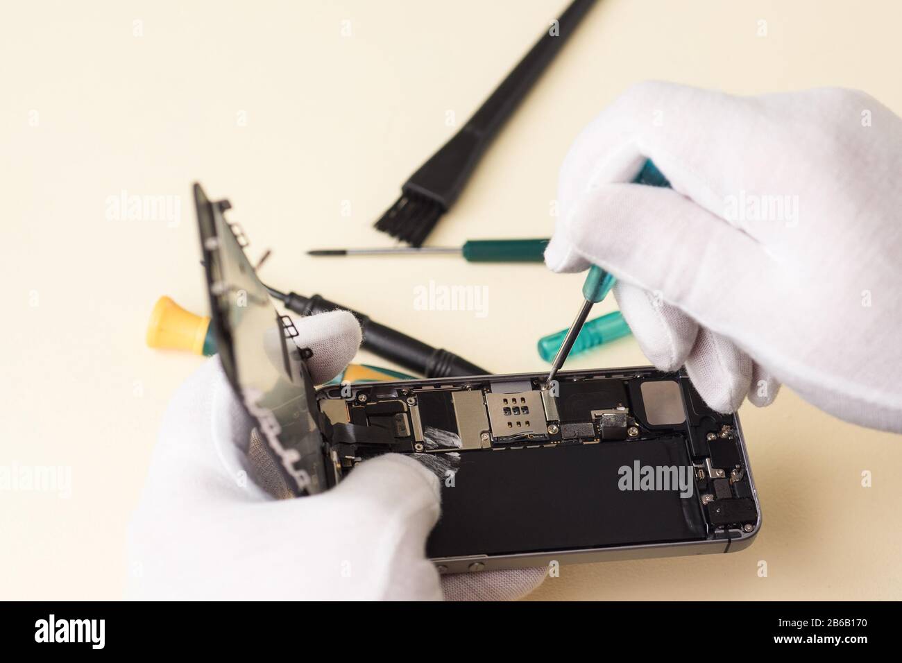 Hands in white gloves with a screwdriver to disassemble the smartphone ...