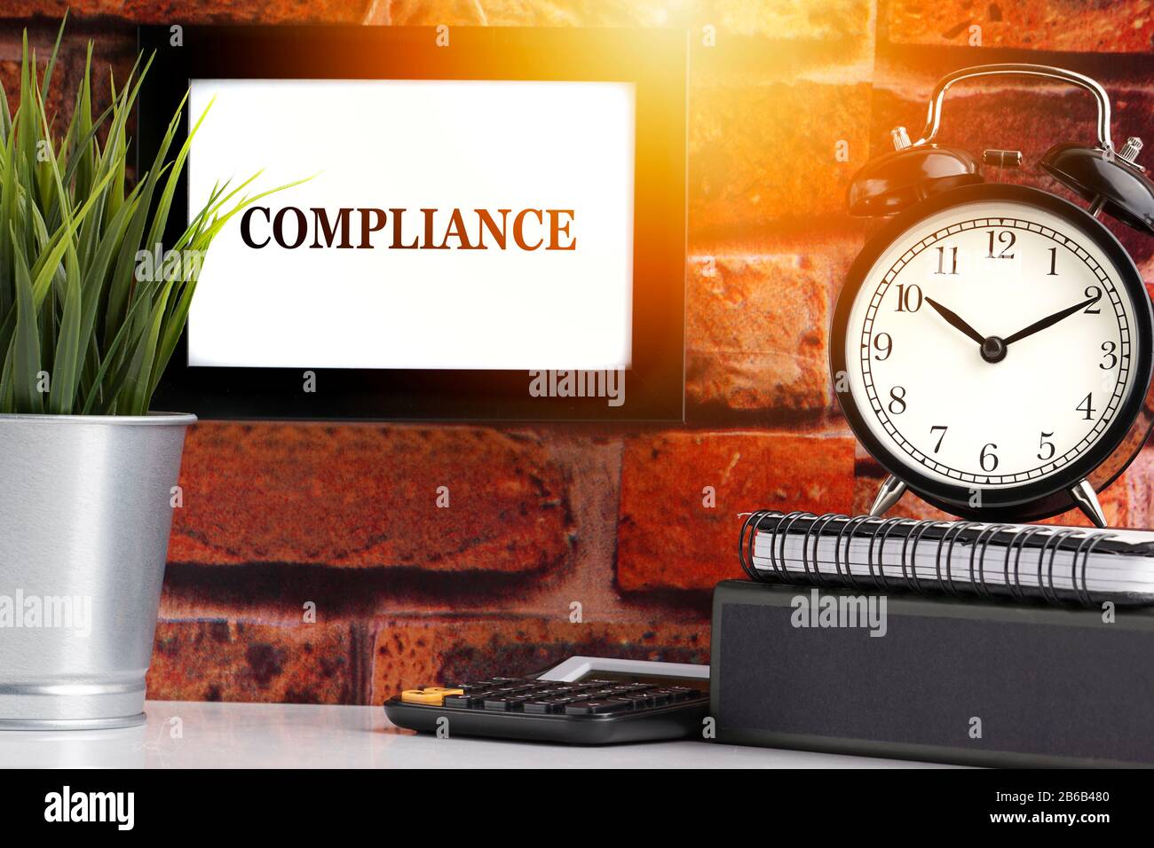 COMPLIANCE text with alarm clock, books and vase on brick background ...
